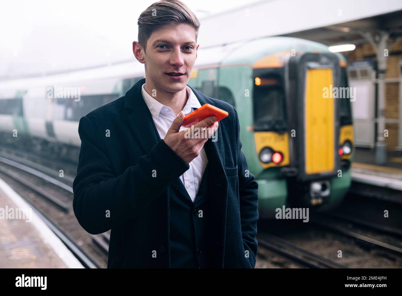 Young businessman talking on speaker phone standing at platform station ...