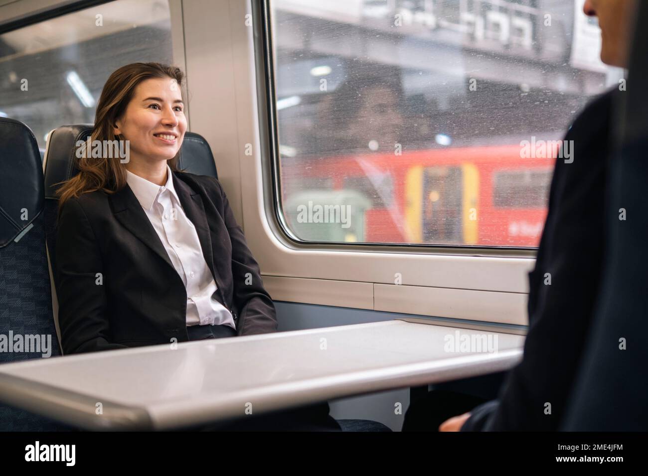 Happy businesswoman with colleague sitting by window in train Stock ...
