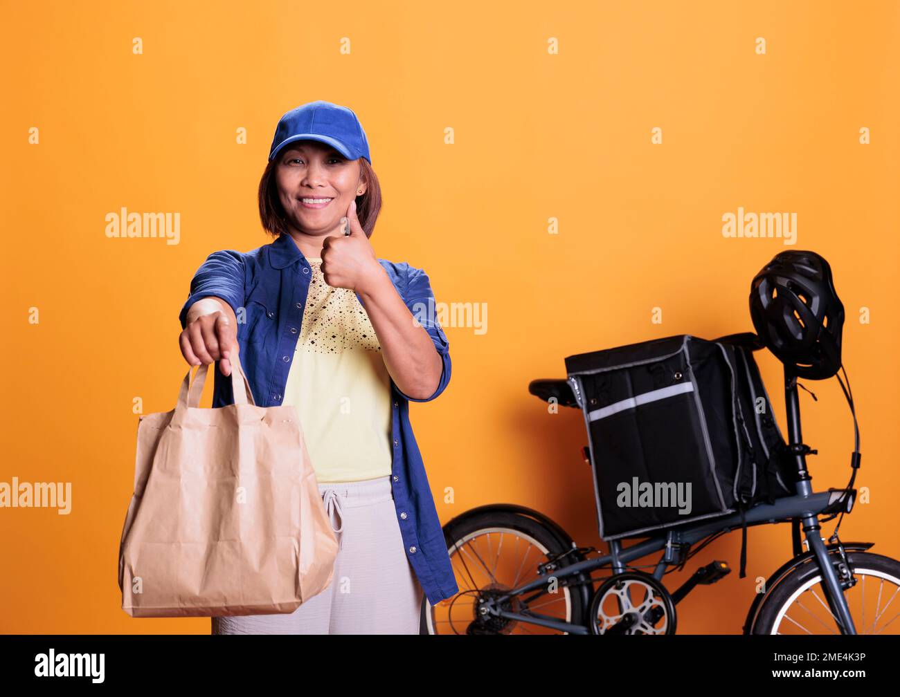 Smiling deliverywoman doing thumbs up gesture while delivering take ...