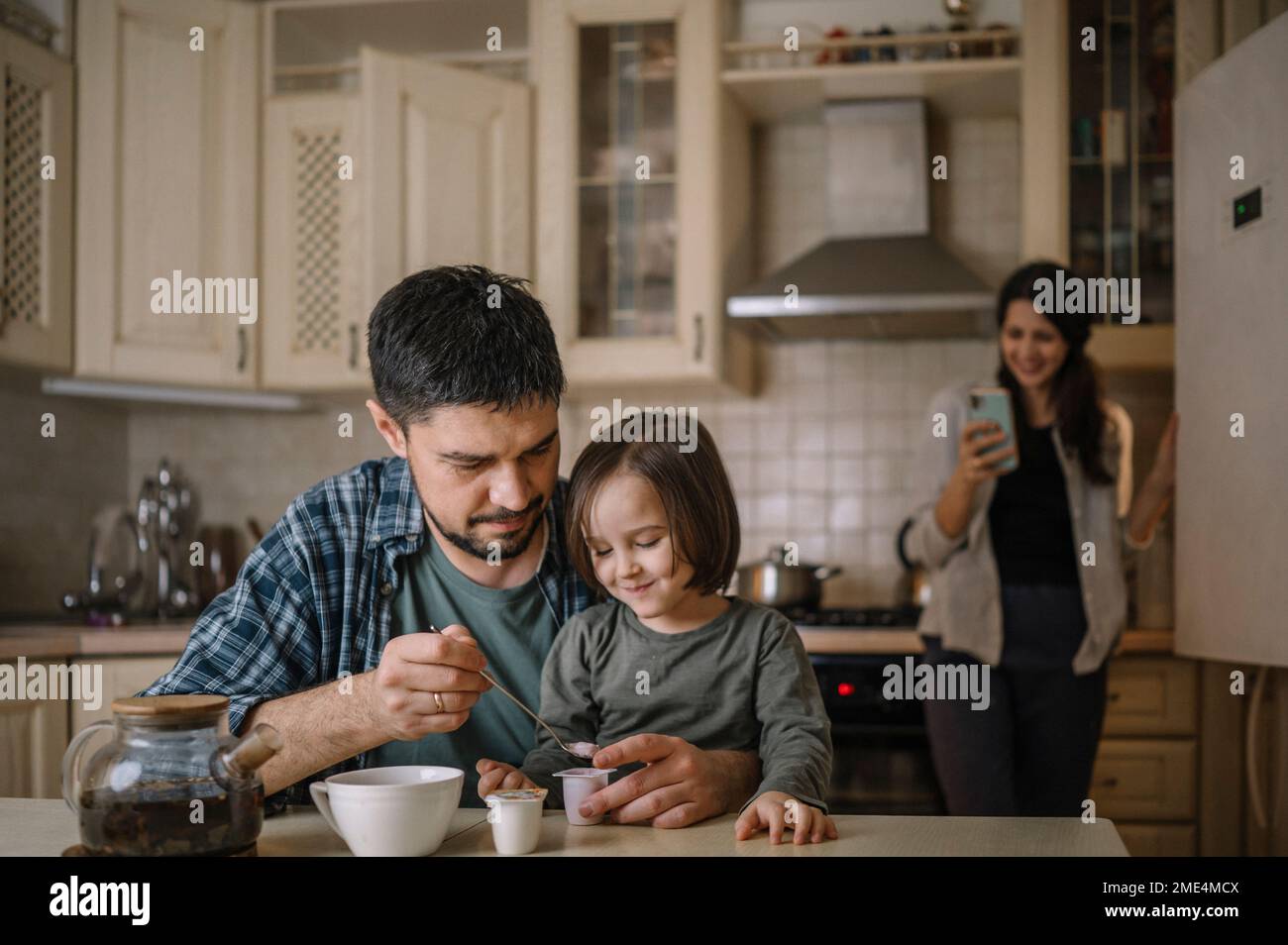 Father and son preparing tea with mother using smart phone in ...