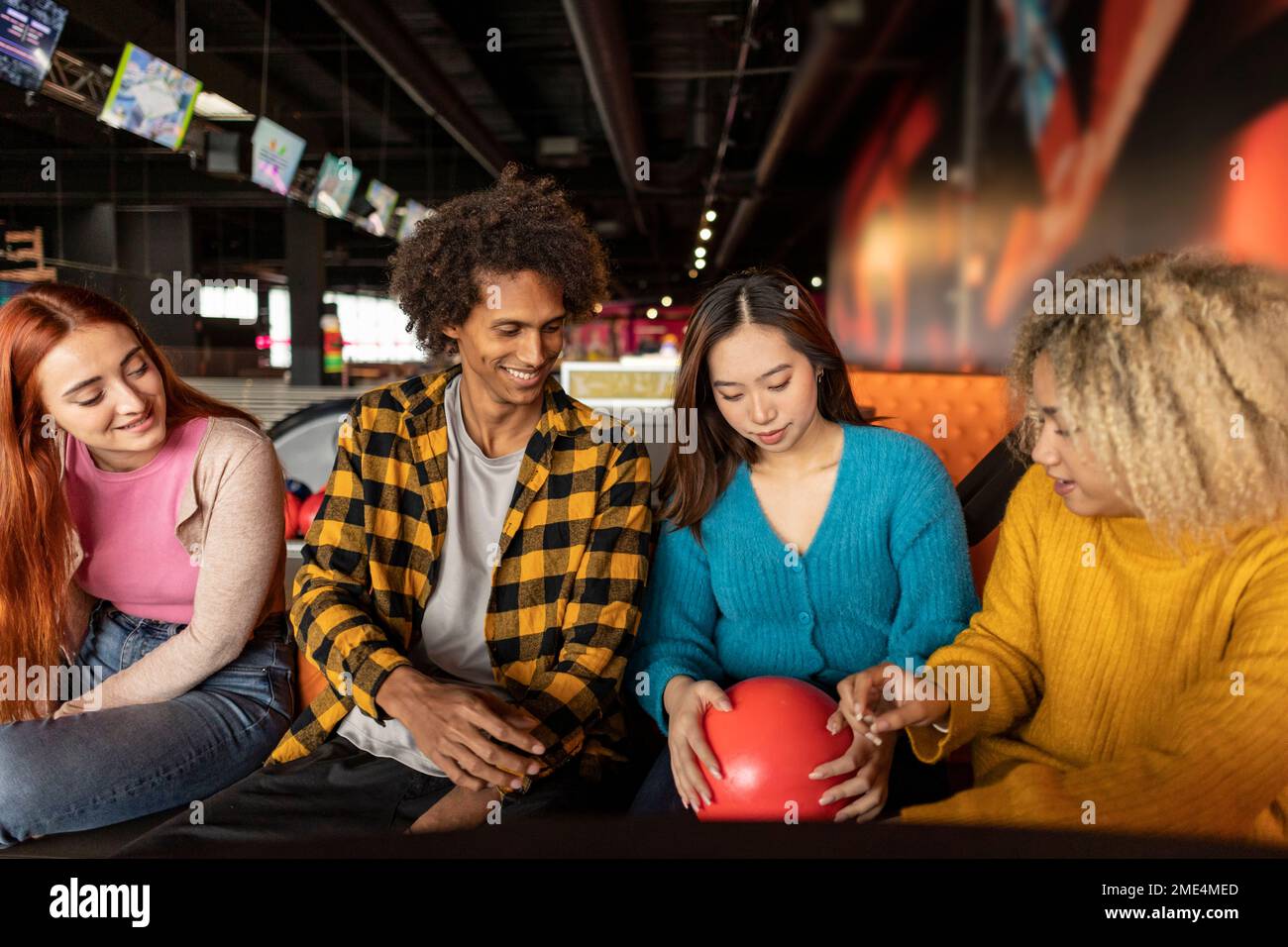 Multiracial friends looking at red bowling ball at alley Stock Photo ...