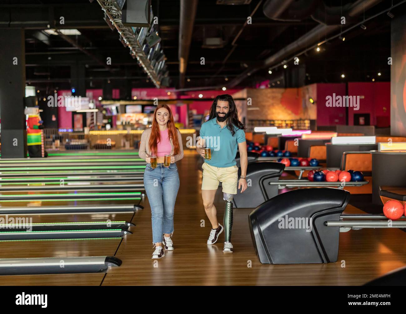 Happy man and woman with glasses of beer walking in bowling alley Stock ...