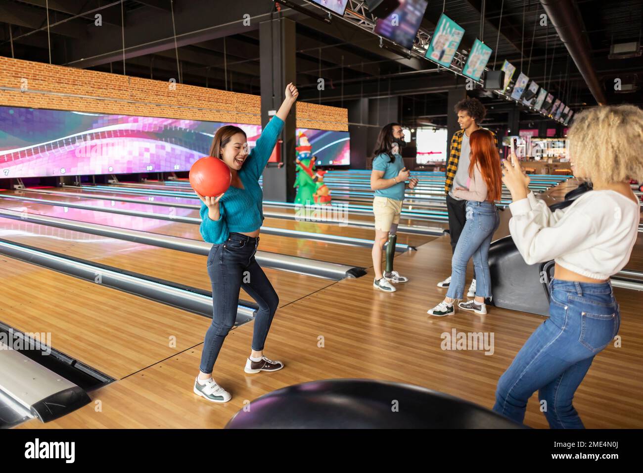 Young woman taking photo of friend holding bowling ball at alley Stock ...