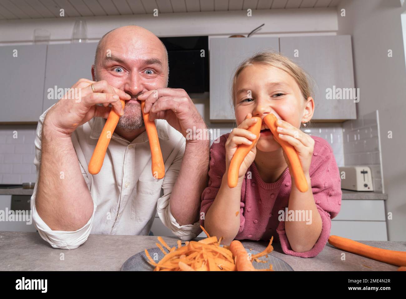 Father and daughter having fun with carrots in kitchen at home Stock ...