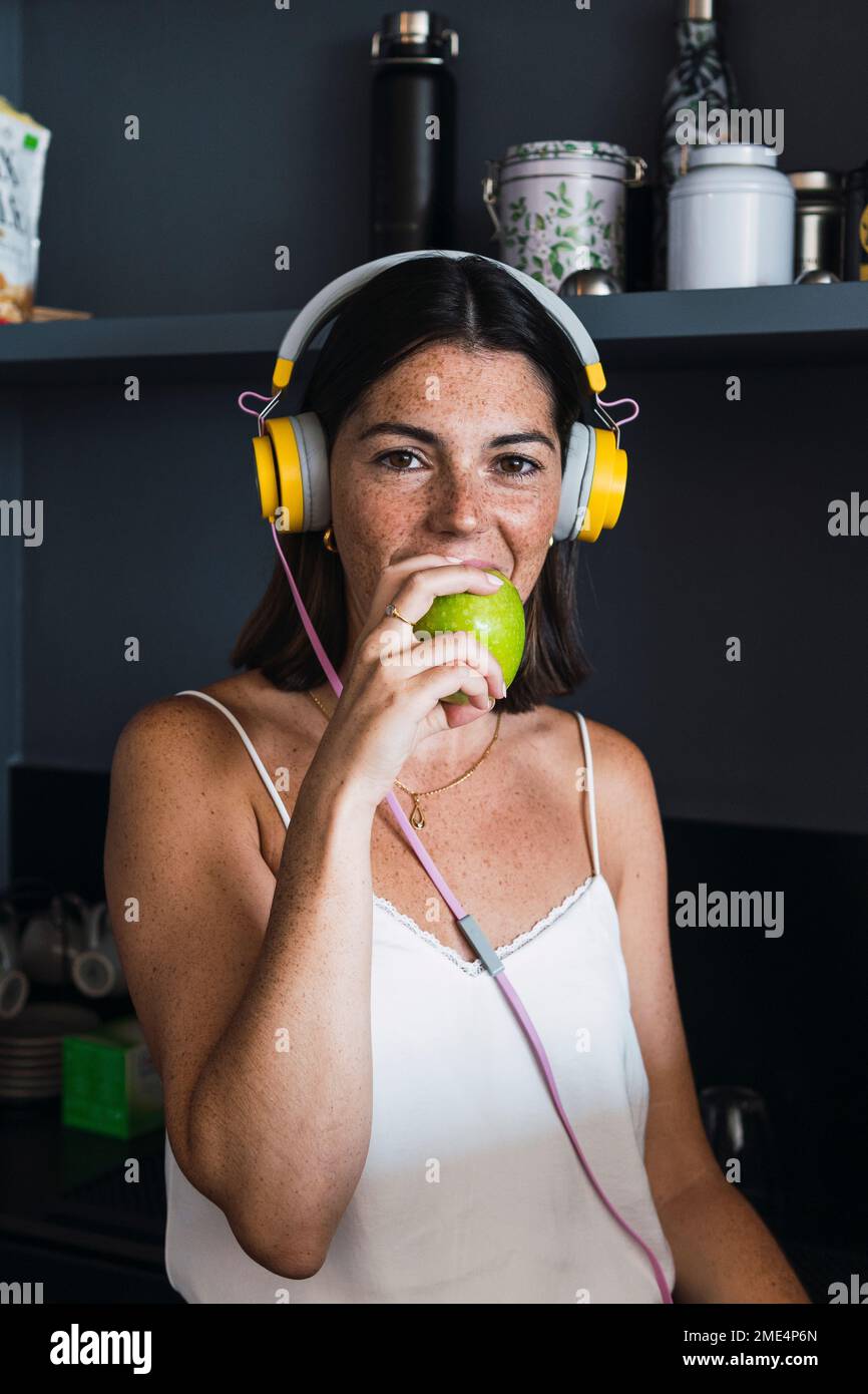 Young woman wearing headphones eating apple at home Stock Photo - Alamy
