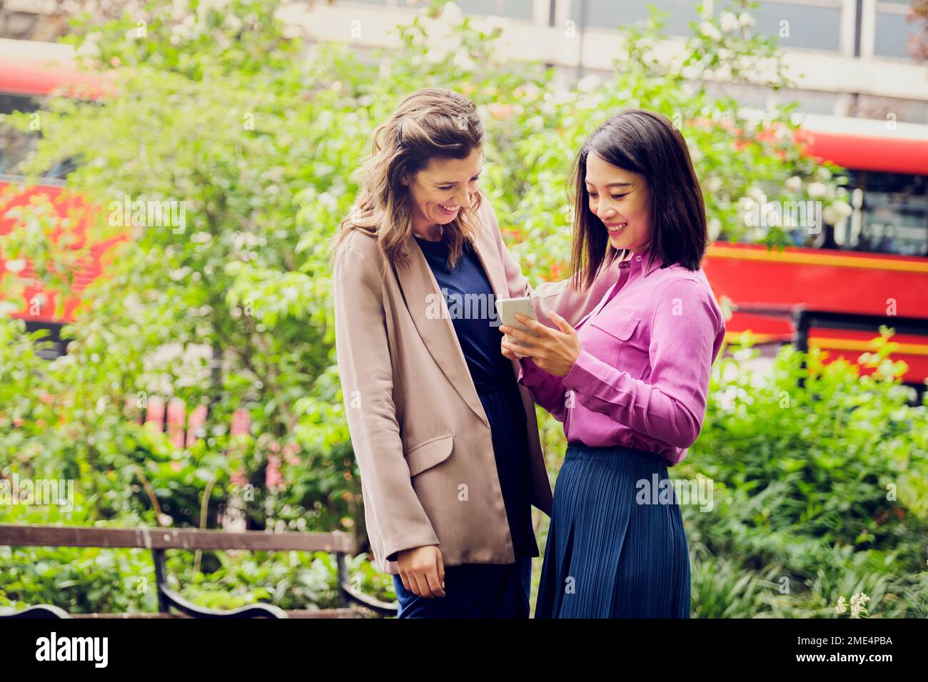 Happy businesswomen using mobile phone with colleague at park Stock ...