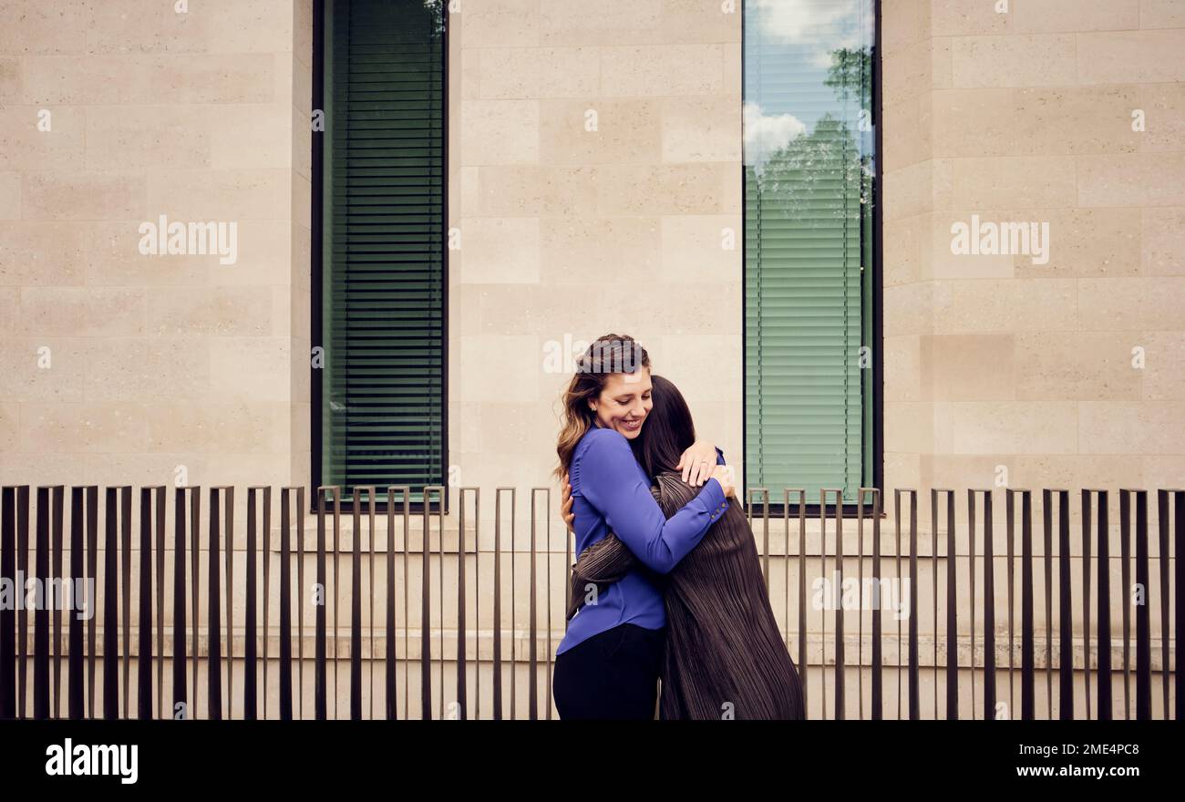 Happy businesswoman hugging colleague standing in front of building ...