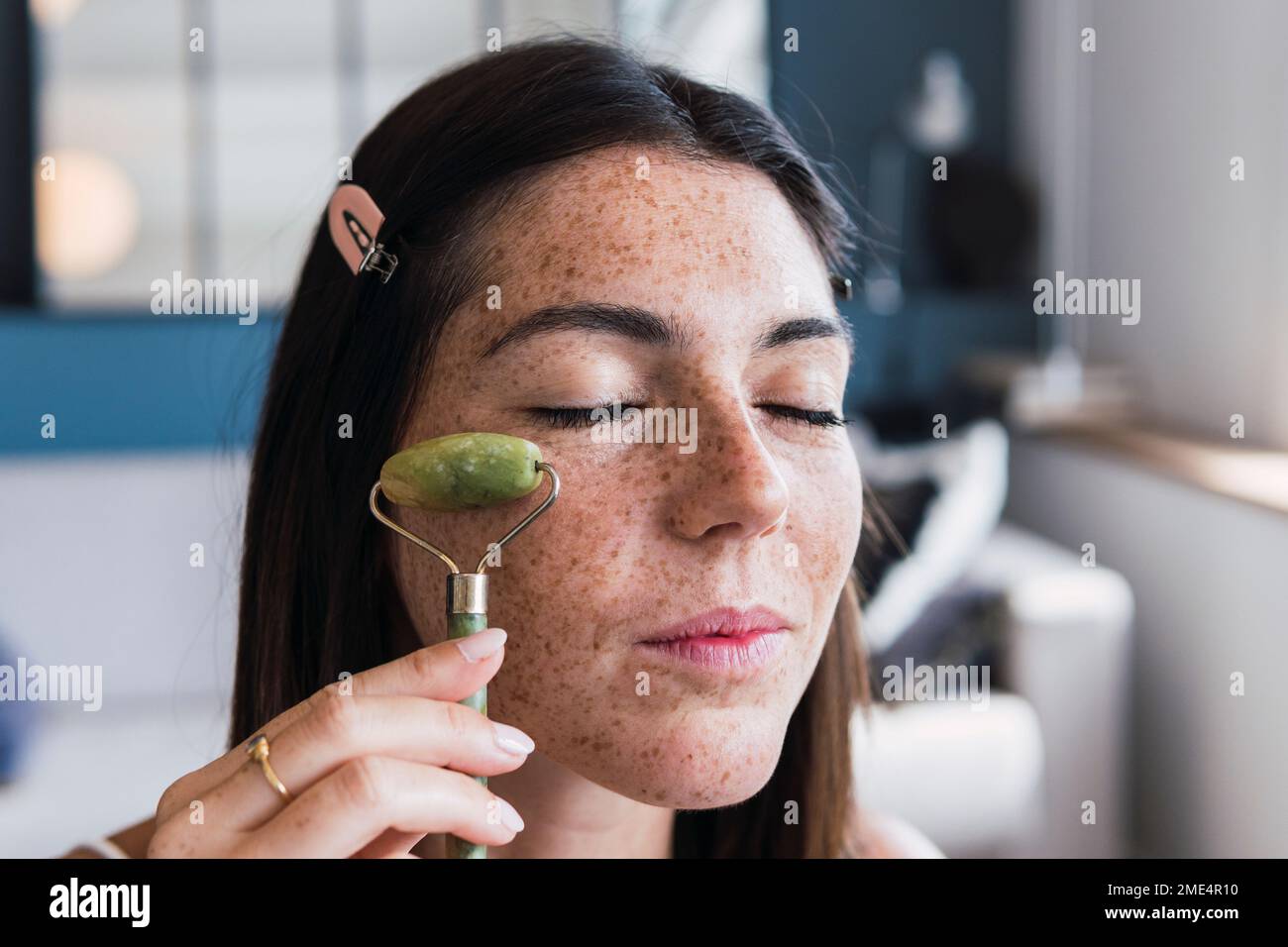 Young woman with freckle face massaging using jade stone roller at home ...