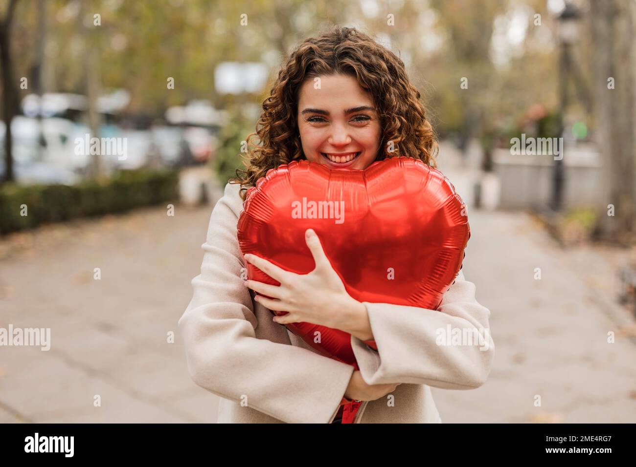 Happy young woman hugging red heart shaped balloon at footpath Stock ...