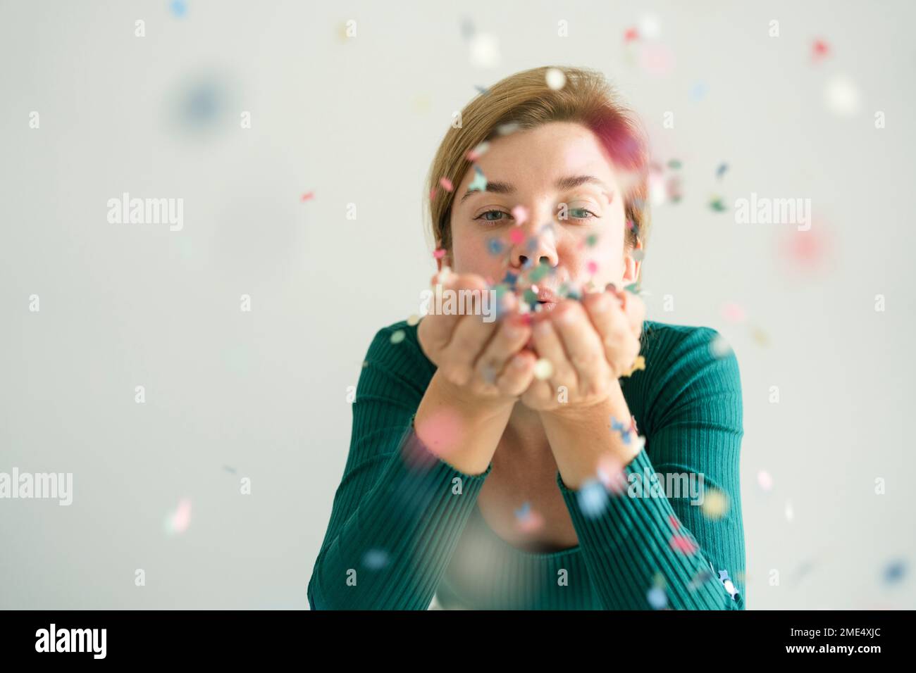 Woman blowing confetti in front of white wall Stock Photo - Alamy
