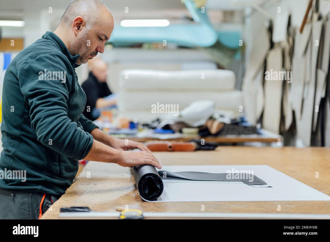 Upholstery worker rolling fabric by table in workshop Stock Photo - Alamy