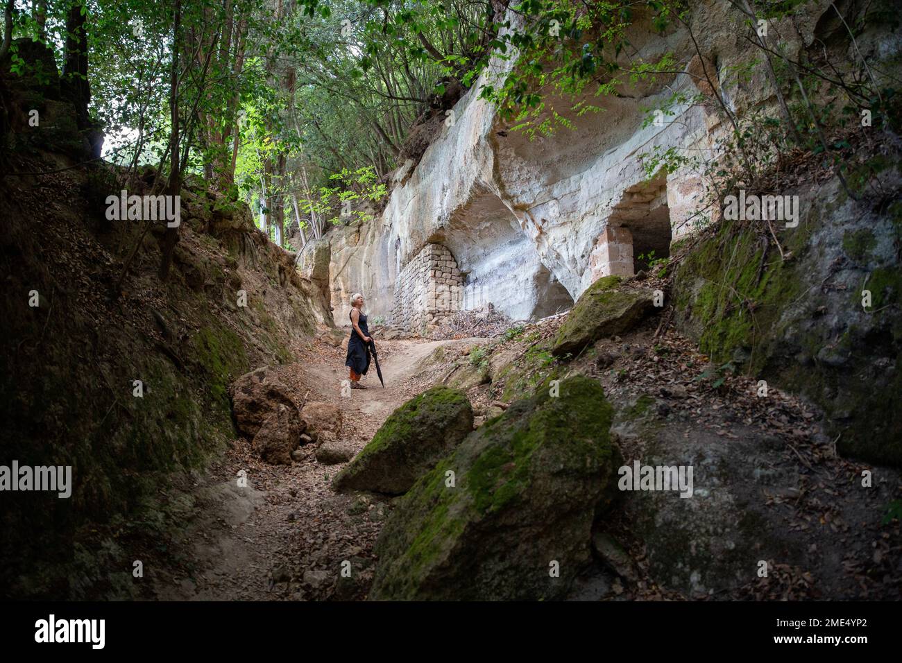 Senior woman standing in front of cave under tree Stock Photo - Alamy