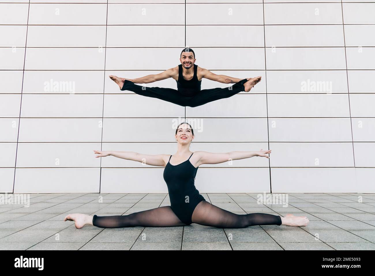 Happy man and young woman doing splits in front of tiled wall Stock ...