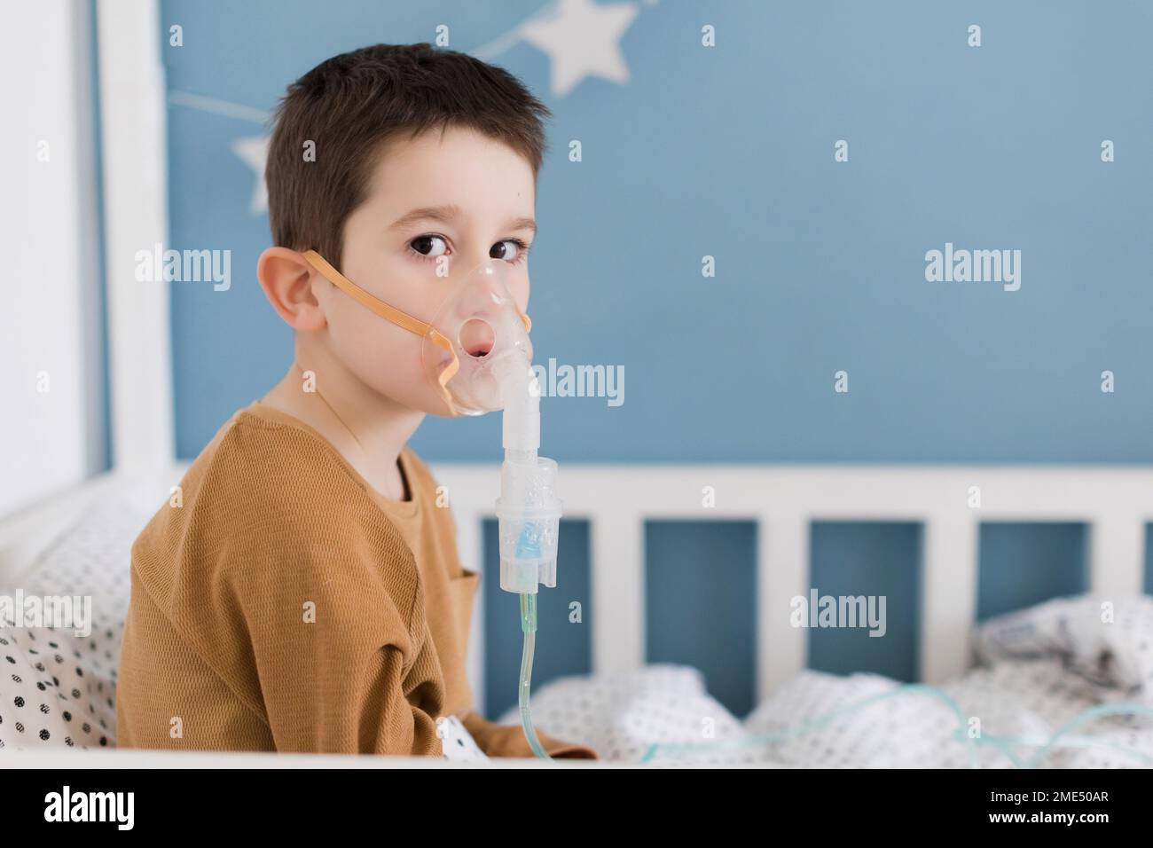 Sick boy wearing nebulizer mask sitting on bed at home Stock Photo - Alamy