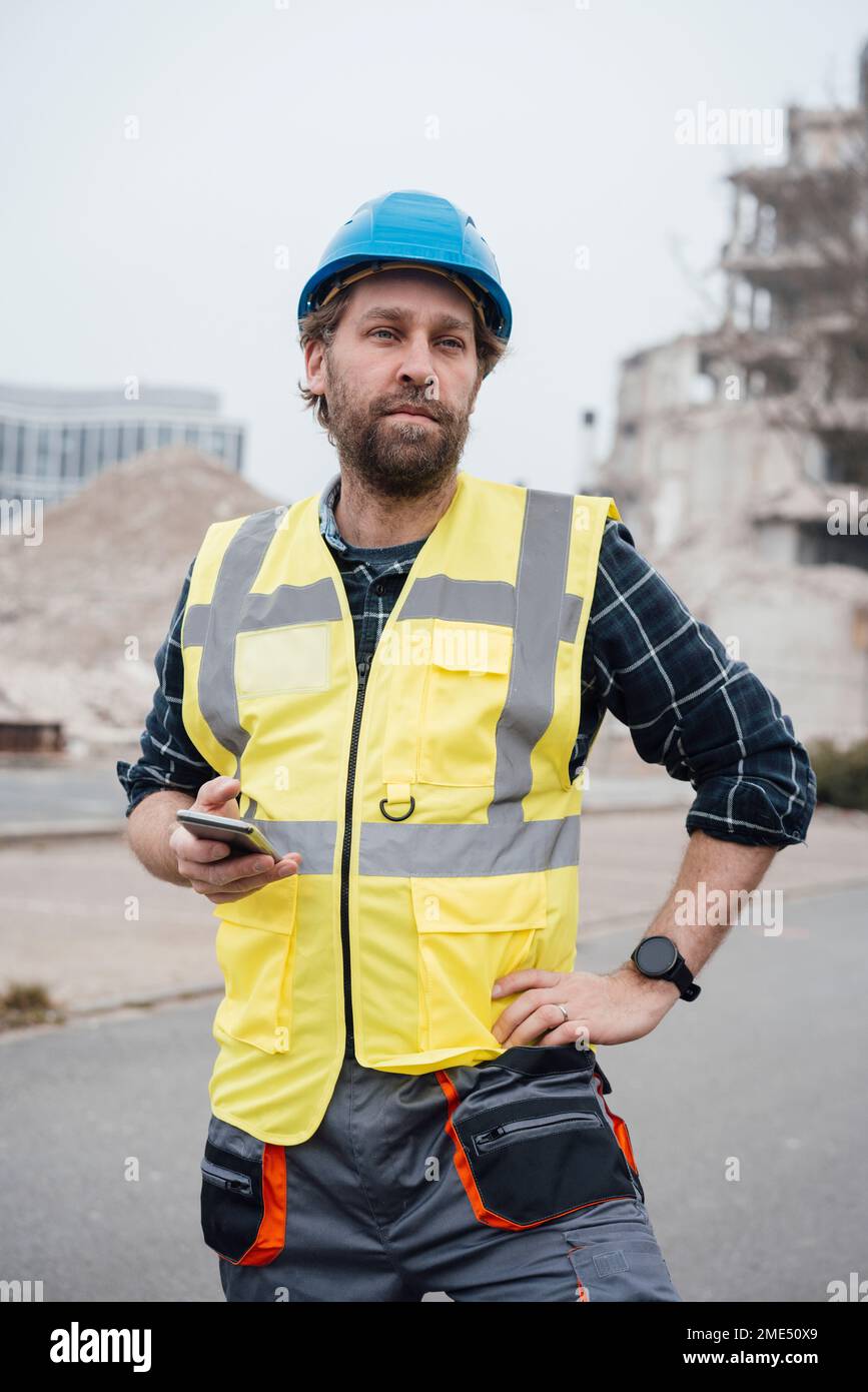 Blue-collar worker holding mobile phone with hand on hip Stock Photo ...