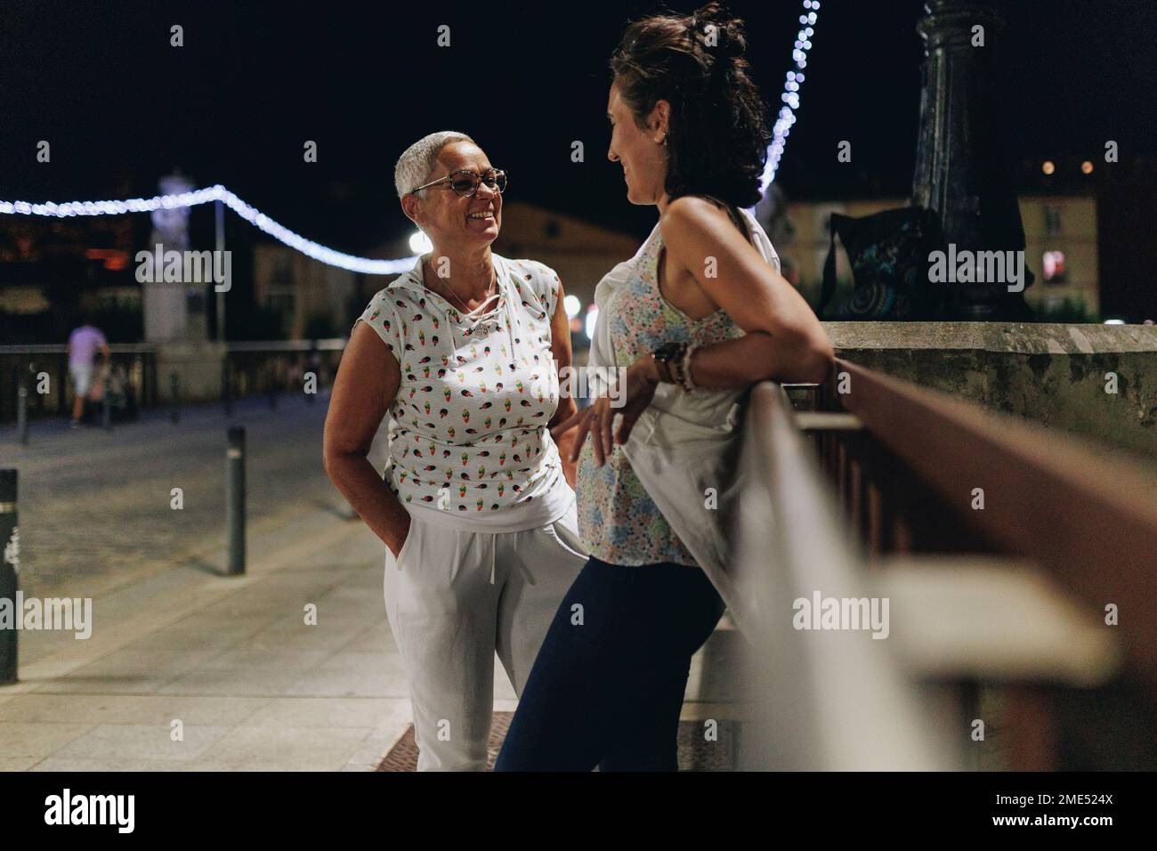 Happy friends talking on bridge at night Stock Photo - Alamy