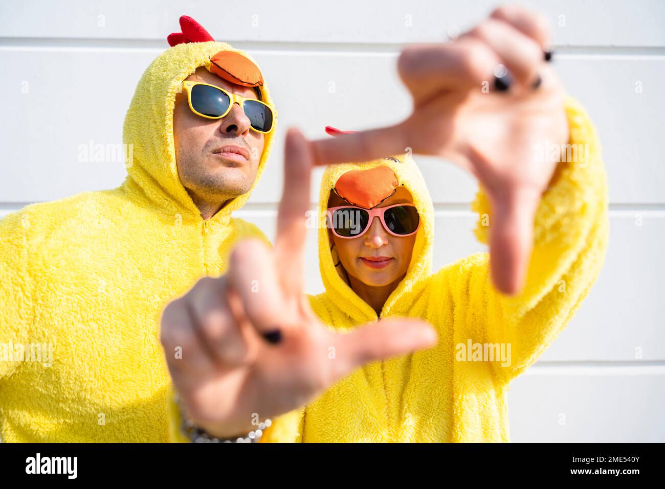 Friends wearing yellow chicken costumes looking through finger frame in ...