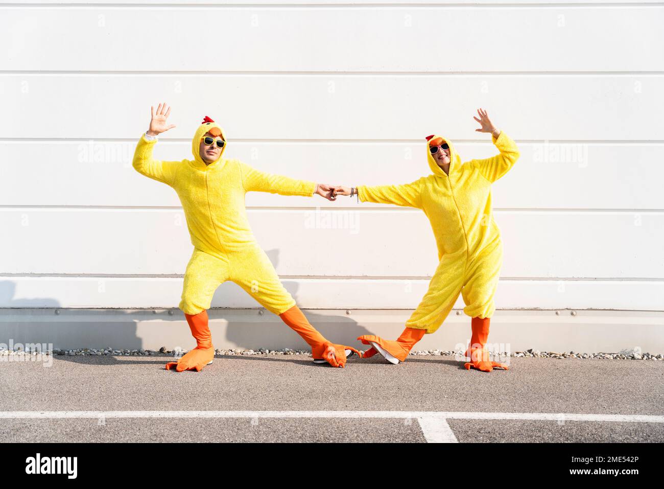 Playful friends wearing chicken costumes holding hands and dancing in ...
