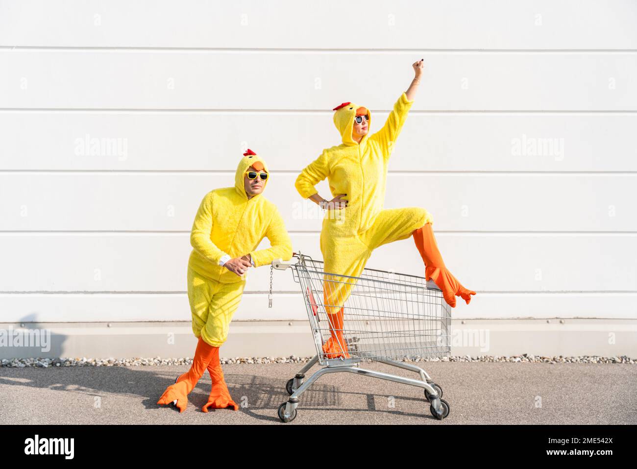 Friends wearing yellow chicken costumes standing with shopping cart in ...
