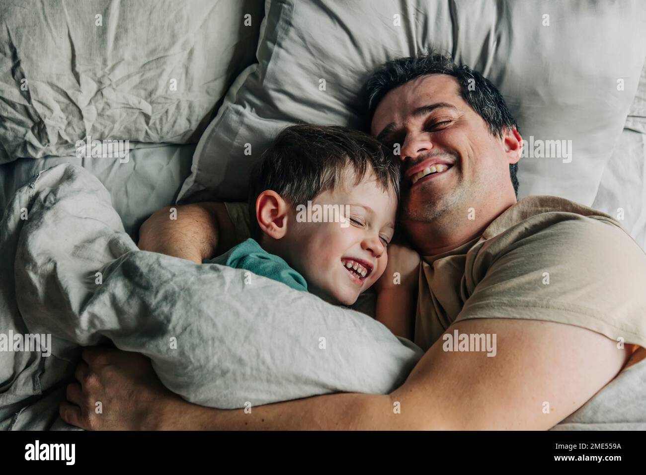 Happy father and son lying on bed in bedroom Stock Photo - Alamy