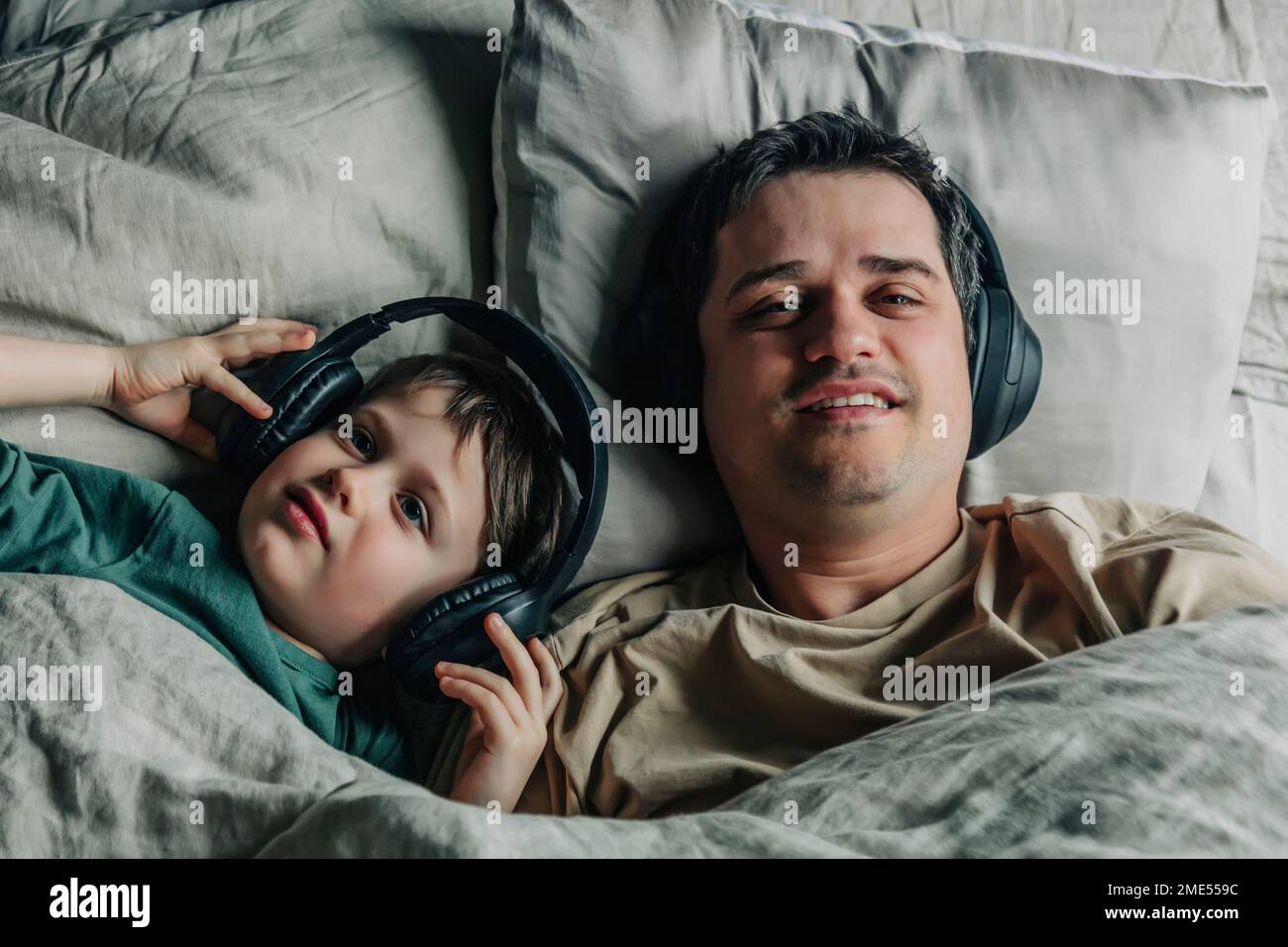 Father and son wearing headphones listening to music on bed Stock Photo ...