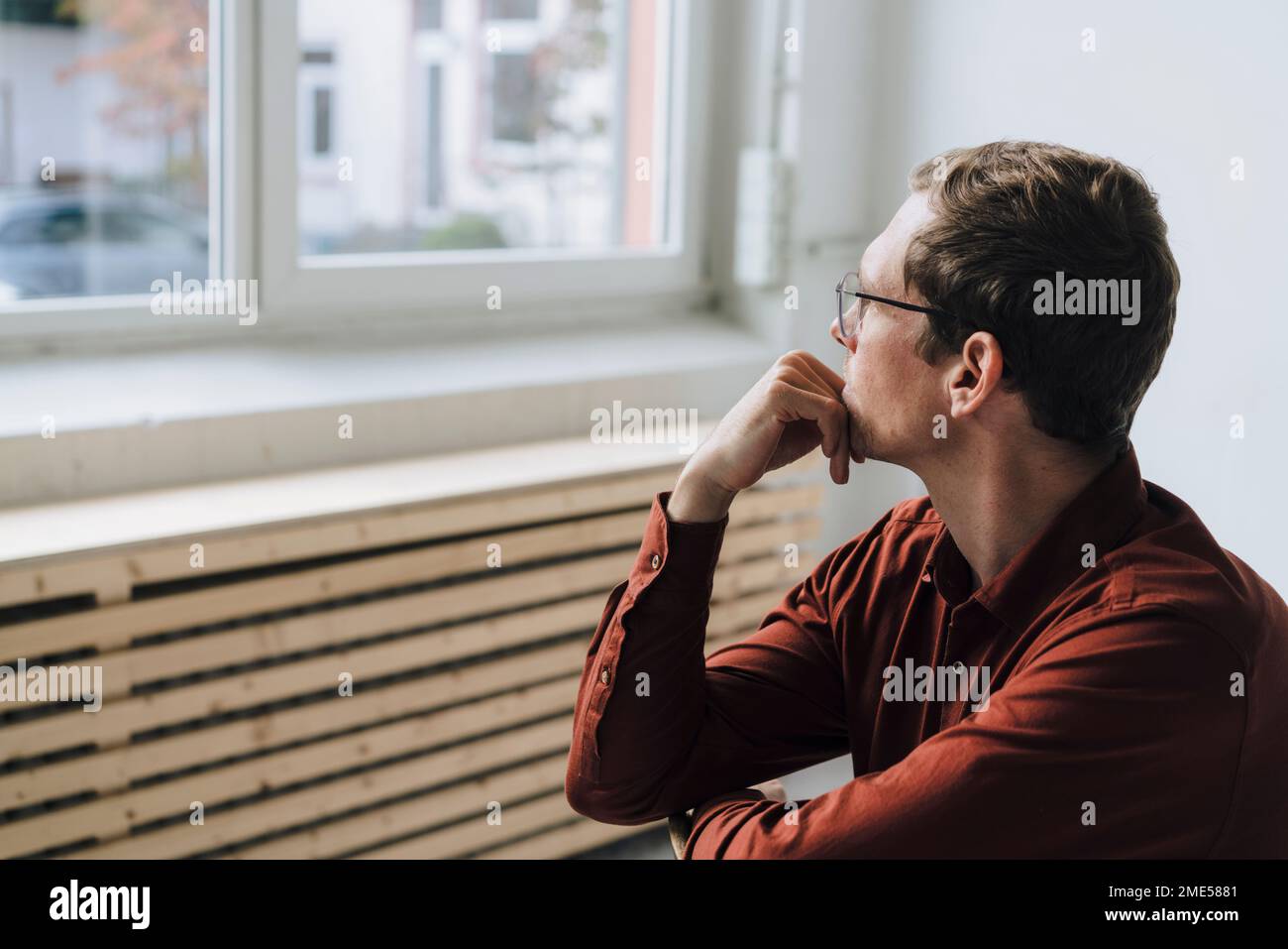 Thoughtful businessman with hand on chin looking through window Stock ...