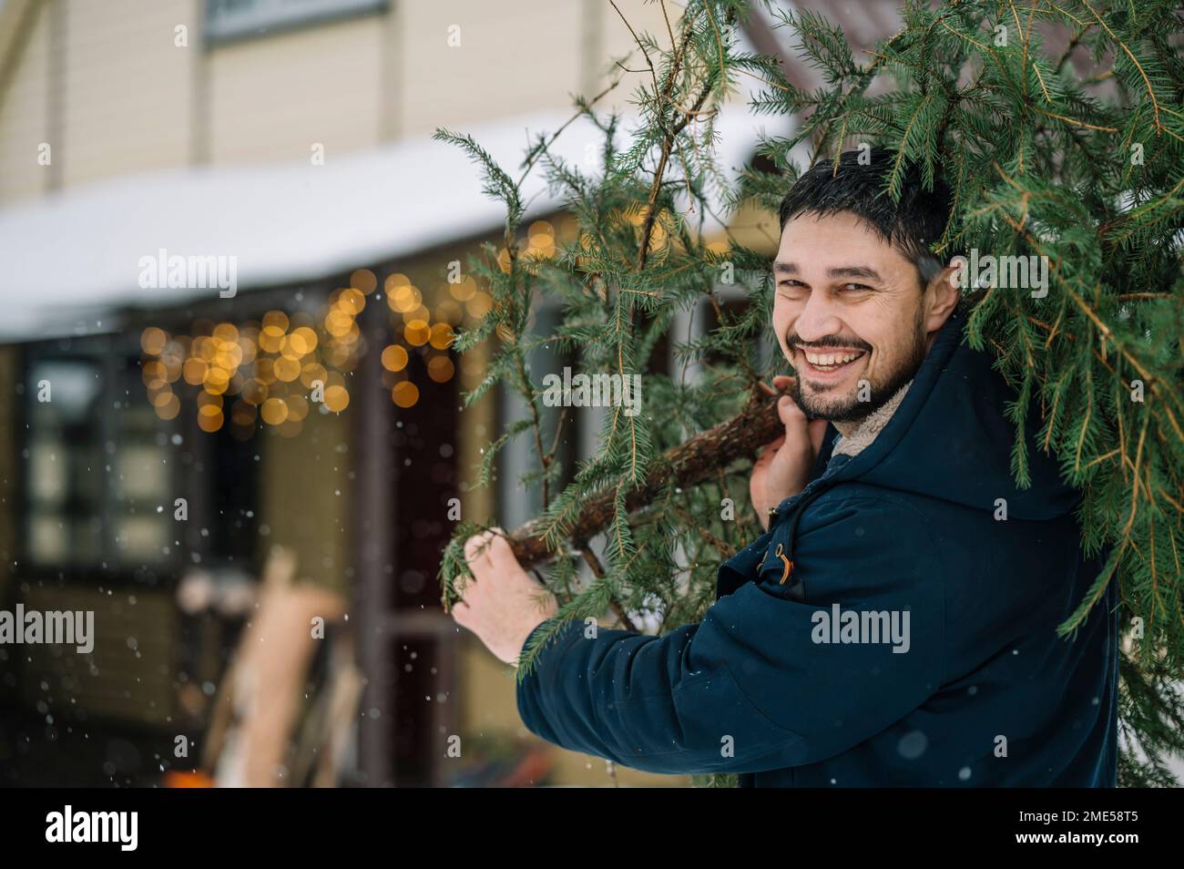 Cheerful man carrying fir tree in front of house Stock Photo - Alamy