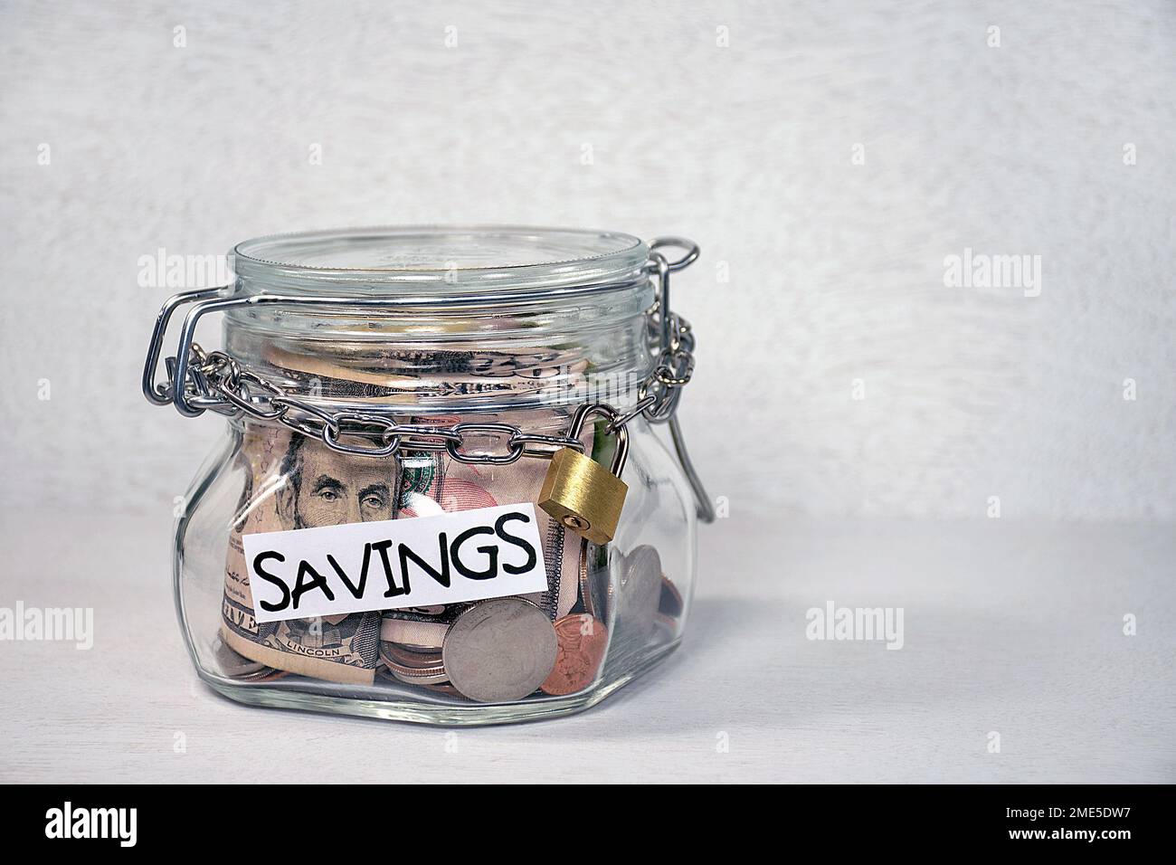 Padlock and chain wrapped around glass jar with savings label and money ...