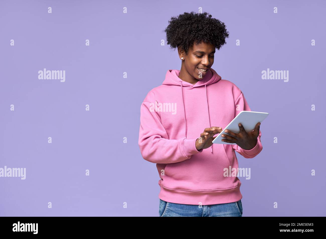 Happy African teenager holding using tablet isolated on purple ...