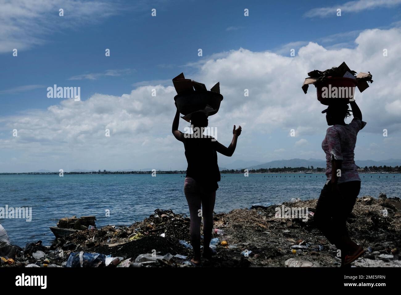 Women carry buckets of trash to the shore on the sidelines of a market ...