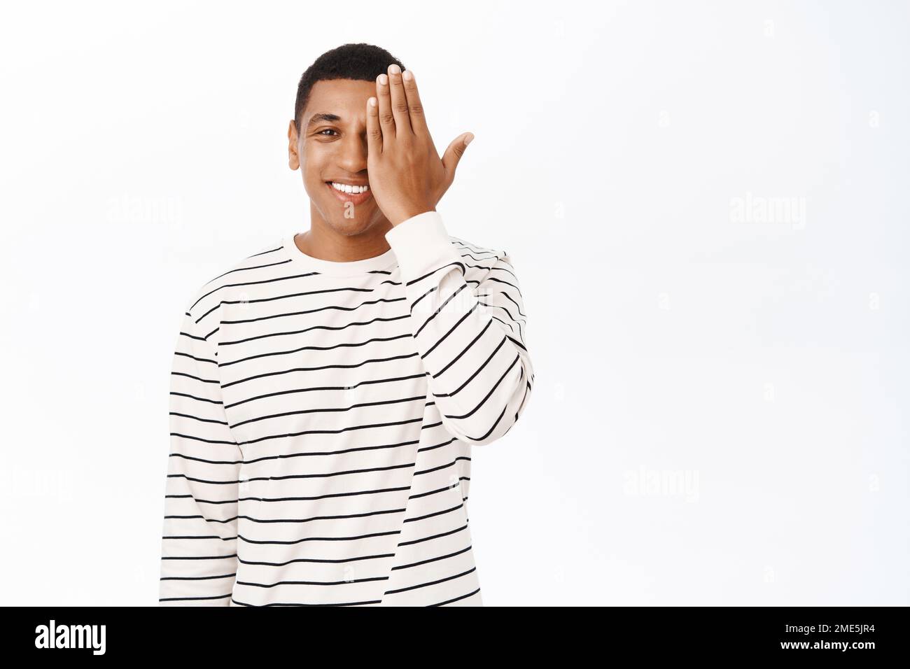 Smiling african american man covers half of face, checks eyes at ...