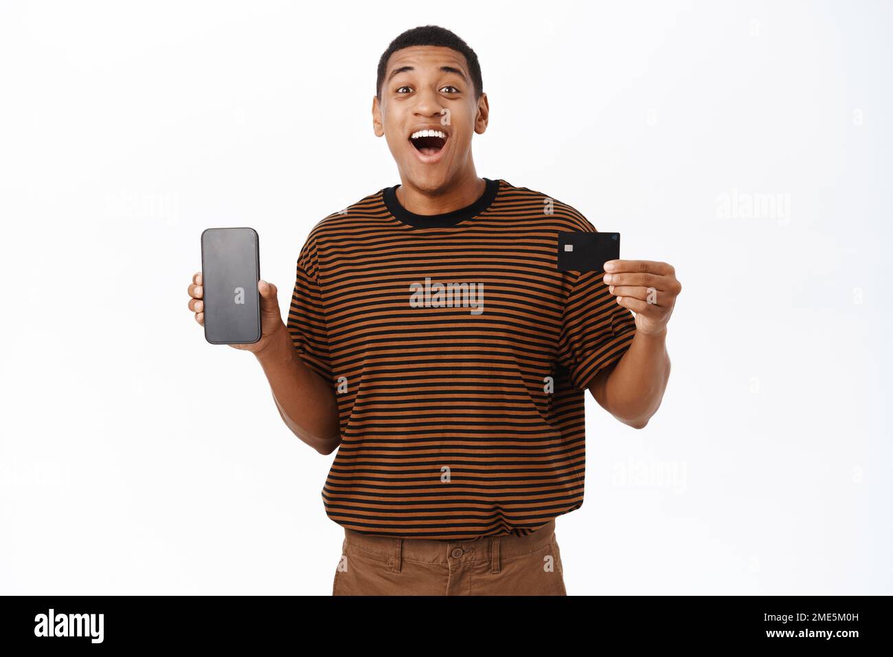 Smiling african american guy showing smartphone screen and credit card ...
