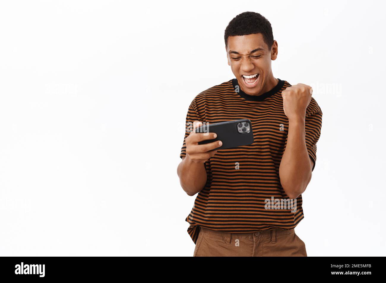 Excited smiling african american man playing on mobile phone, looking ...