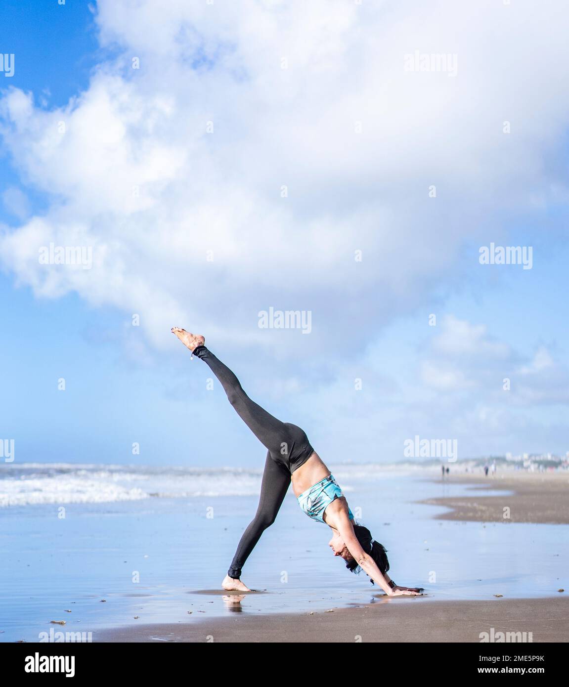 A Woman Practicing Yoga On The Water At The Beach Doing Three Legged