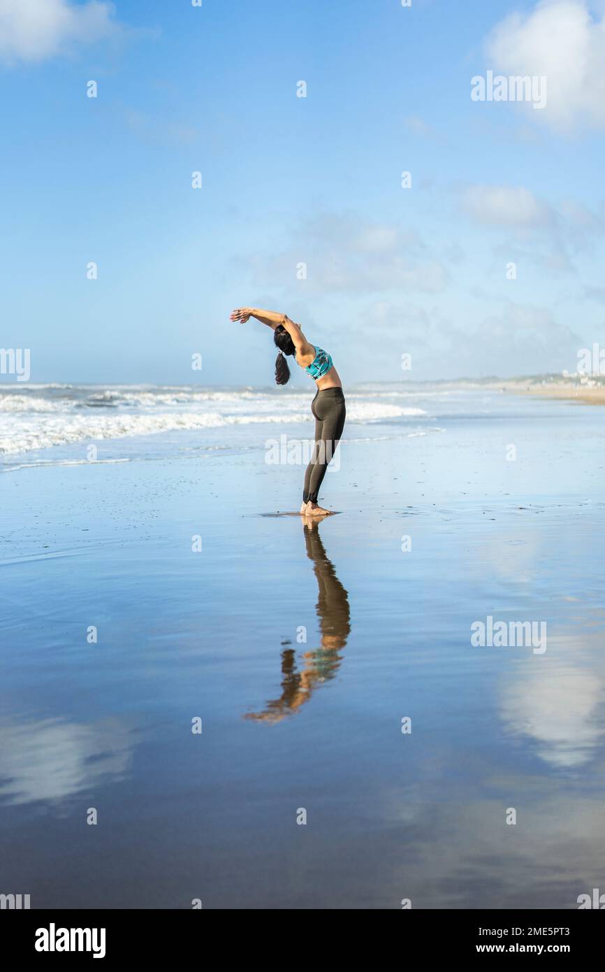 A woman practicing yoga on the water at the beach, doing Mountain with ...
