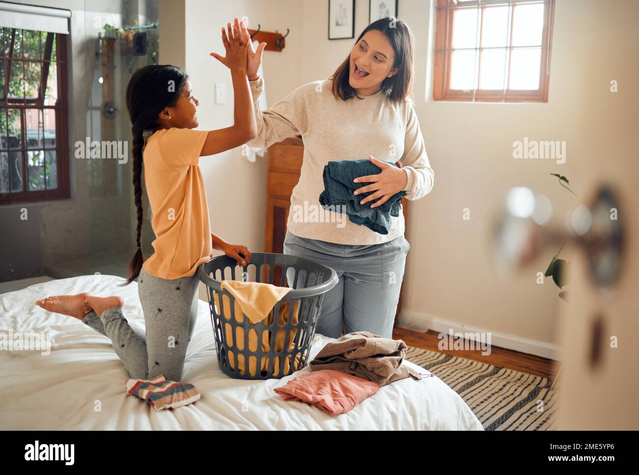 Cleaning, high five and child and mother doing laundry clothes, house work and fold clean fabric ...
