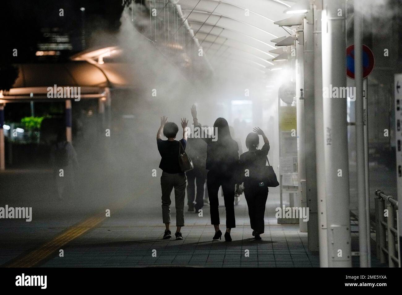 Commuters reach to feel the mist spray as they walk toward a train ...