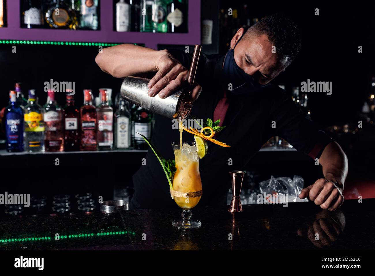 A young professional bartender prepares cocktails for his clients at ...