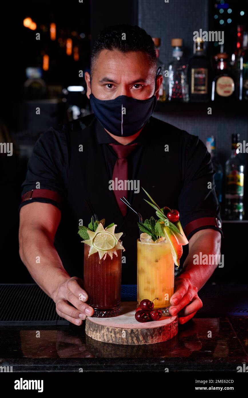 A young professional bartender prepares cocktails for his clients at ...