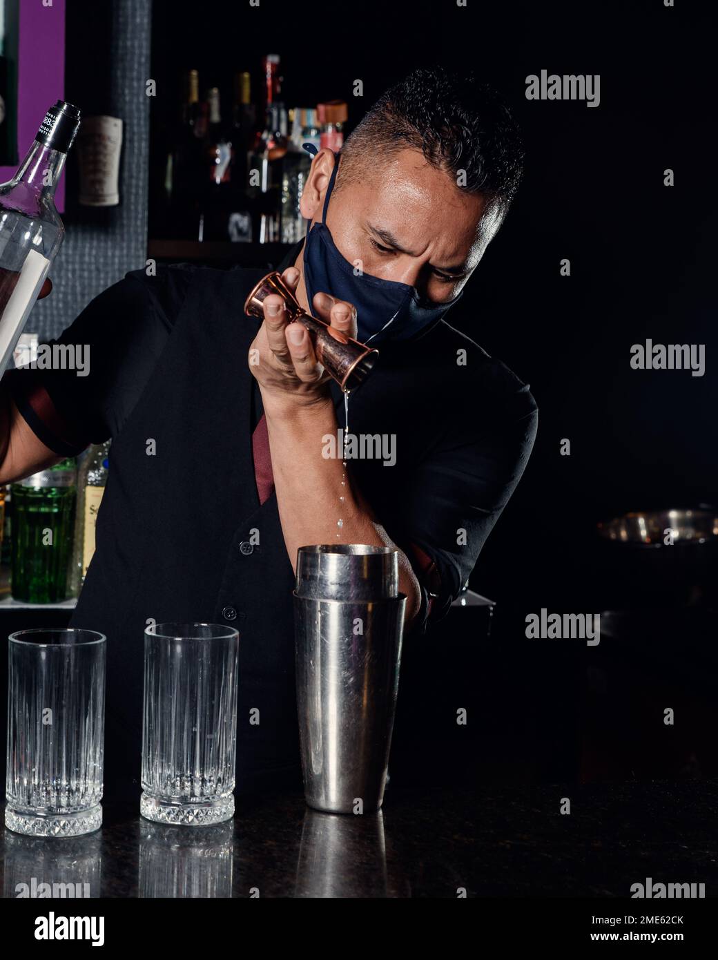 A young professional bartender prepares cocktails for his clients at ...