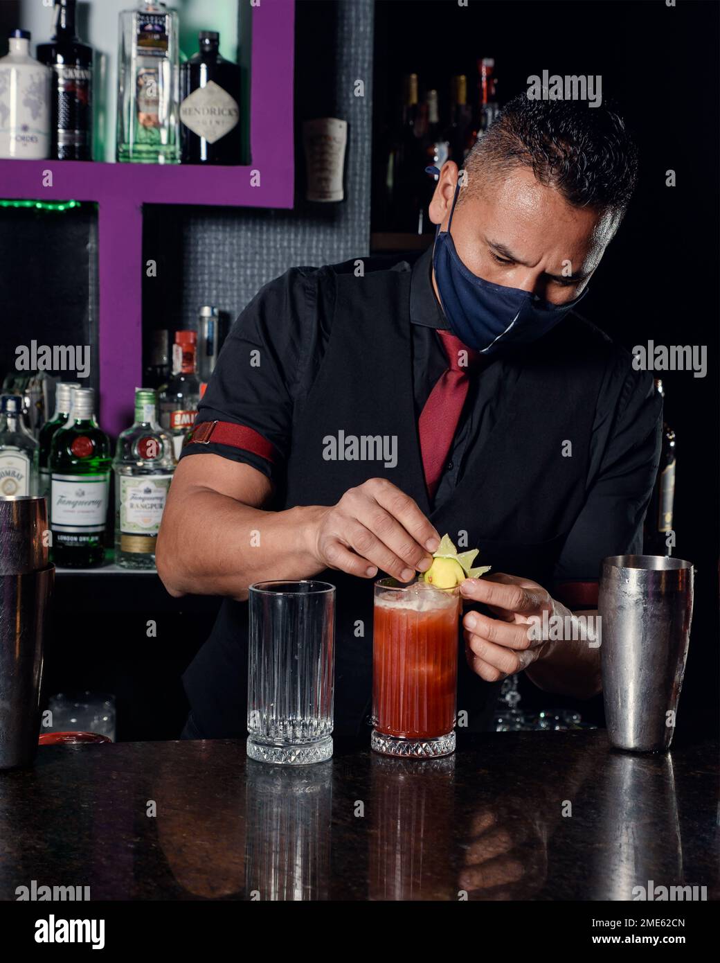 A young professional bartender prepares cocktails for his clients at ...