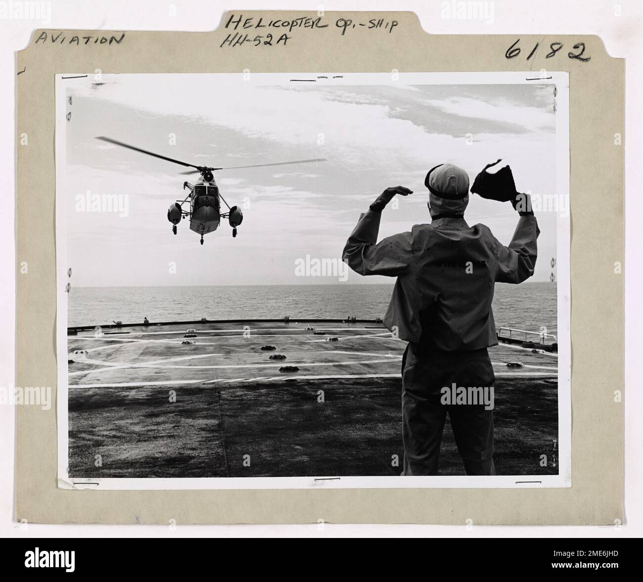 A crewman signals an HH-52A helicopter to land on the flight deck of an ...