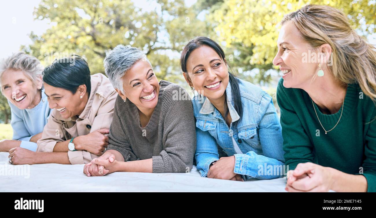 Happy, women and relax at a park, laughing and bonding while lying on a blanket together ...