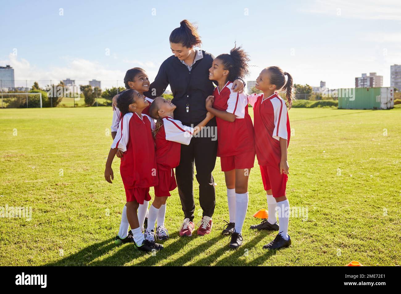 Girl, soccer group and field with coach, team building hug and ...