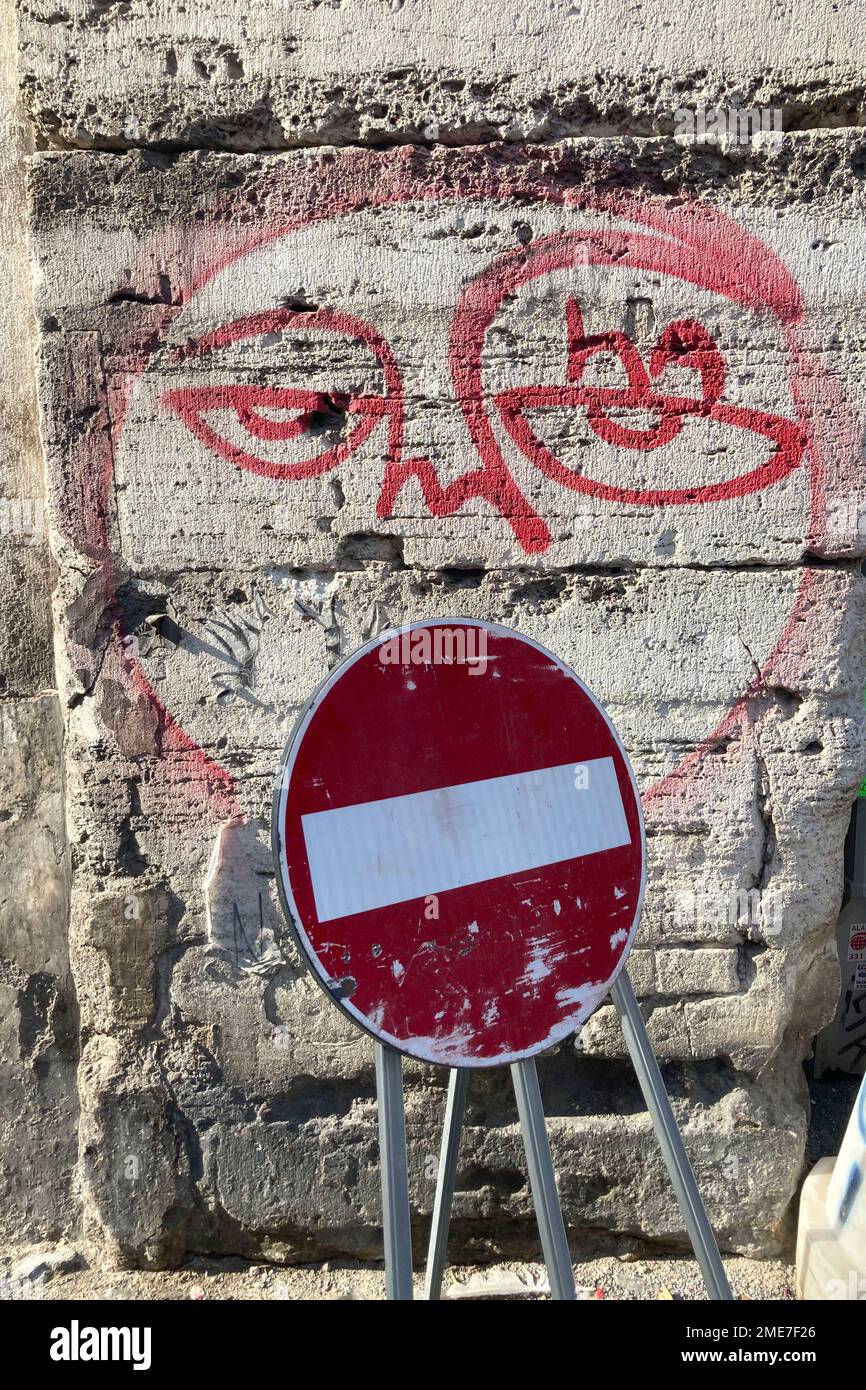 A no entry sign is placed in front of a wall with graffiti on it, in ...