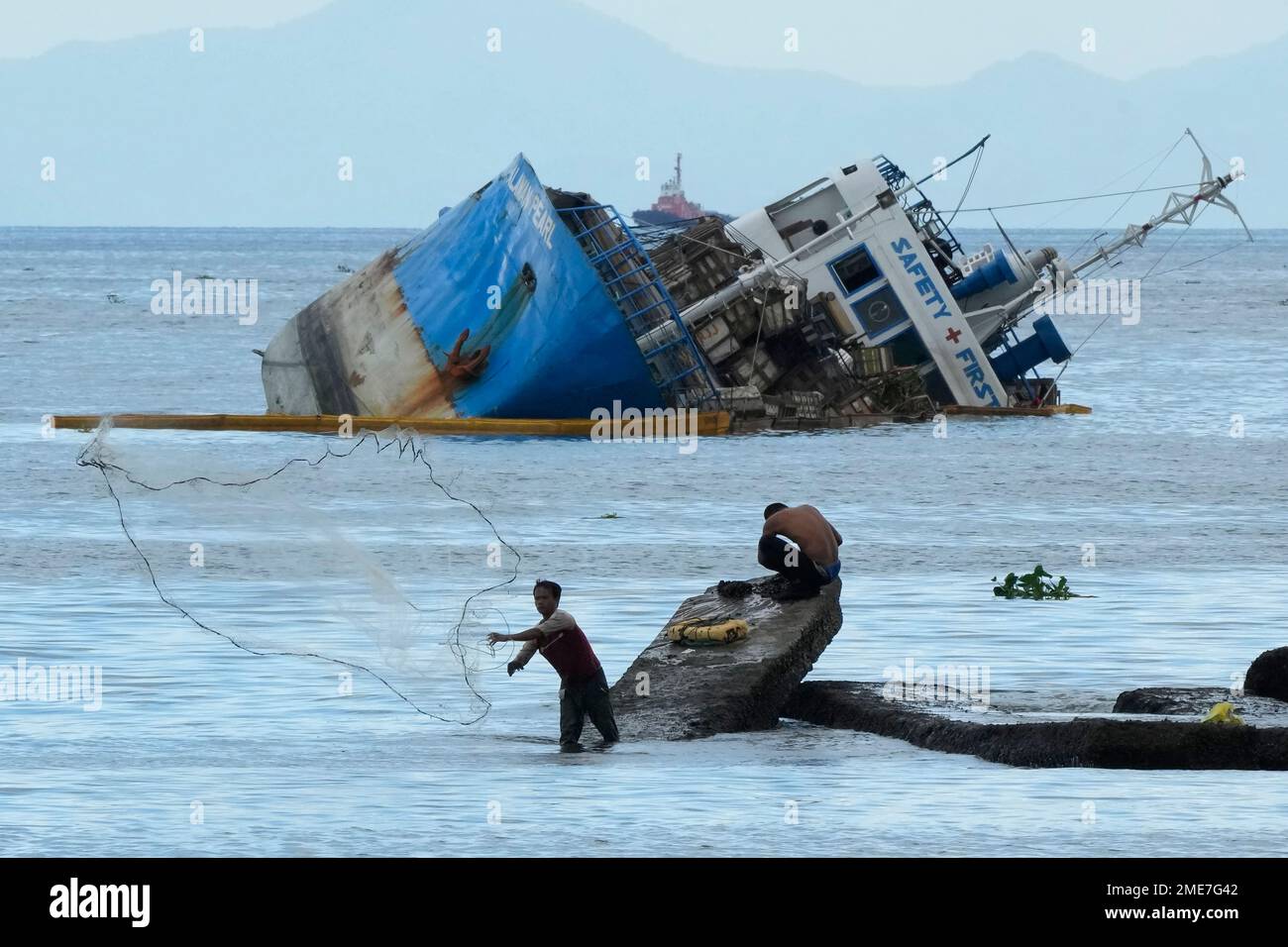 A fisherman throws his net beside the half-submerged M/V Palawan Pearl ...