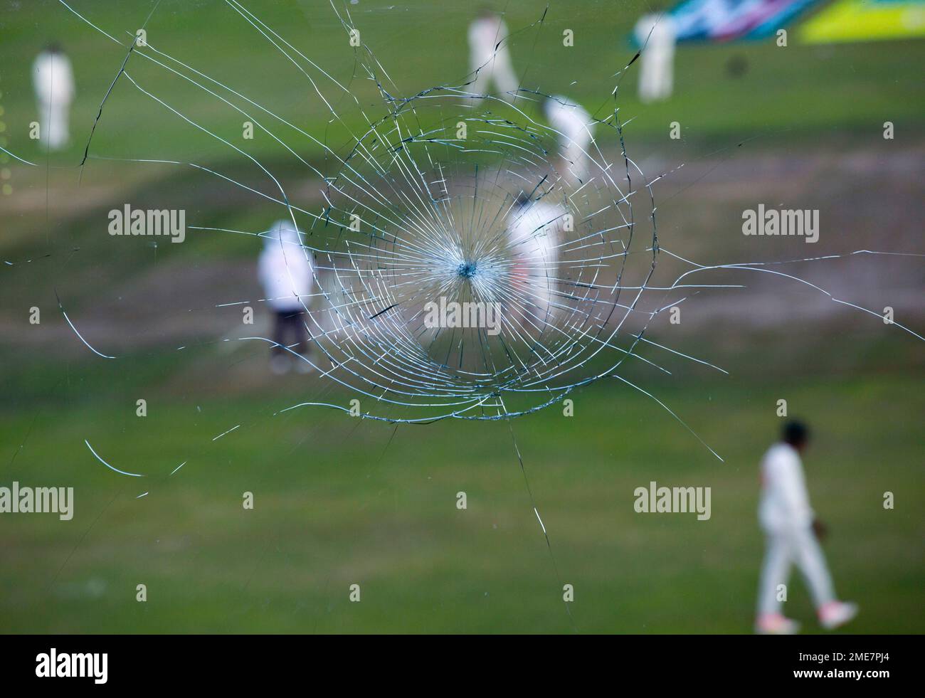 Cricket players are seen on the pitch through a shattered window glass ...