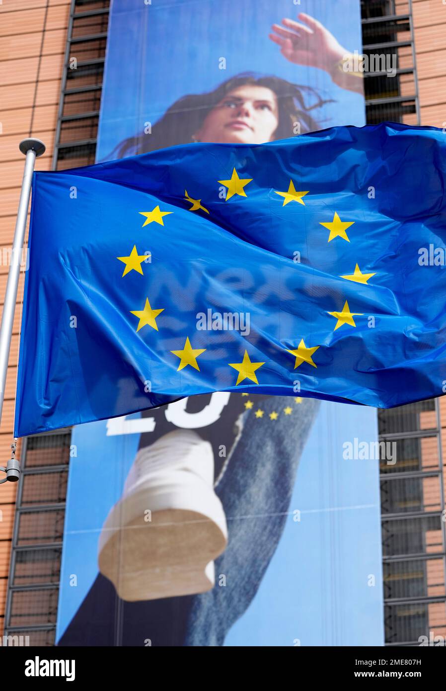 The European Union flag flaps in the wind in front of a giant banner ...