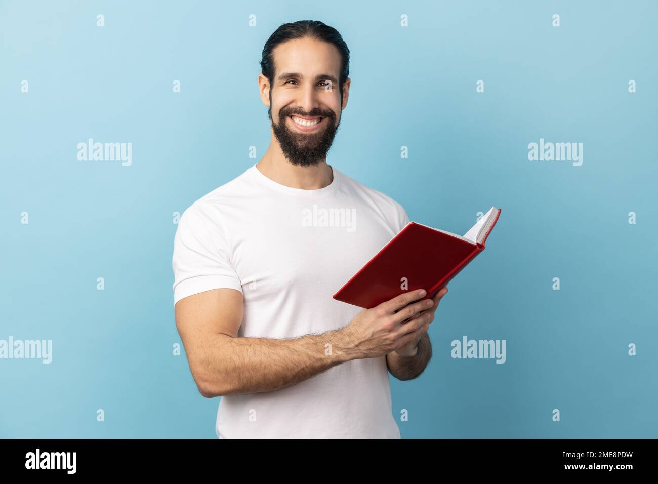 Portrait of man with beard wearing white T-shirt holding book with ...