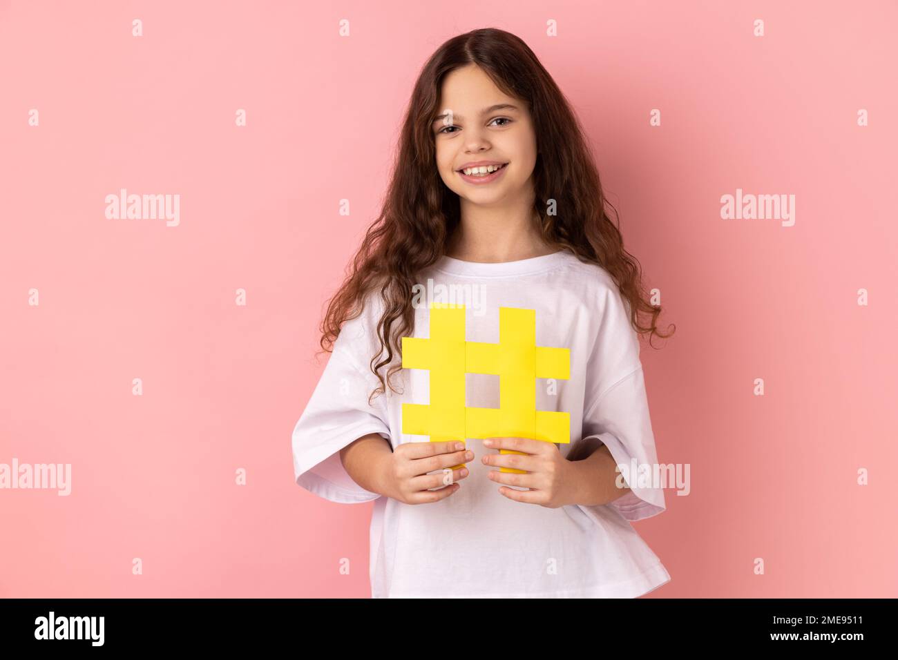 Portrait of adorable little girl wearing white T-shirt holding hashtag ...